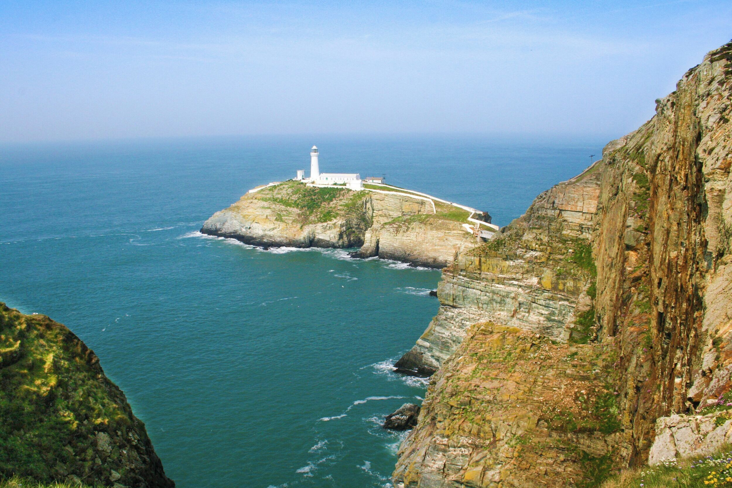 Paisagem costeira com um farol numa rocha, com vista para o mar.