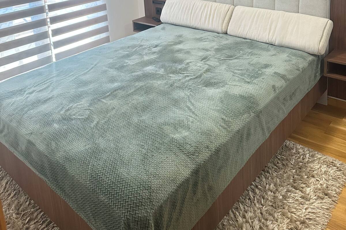 Um quarto com uma cama, mesa de cabeceira, quadro e janela com persianas.