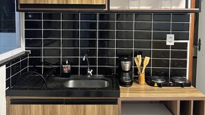 Uma cozinha compacta com painel de azulejos pretos, armários de madeira, pia embutida, cafeteira e geladeira branca.
