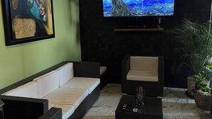Uma sala de estar com sofá, poltronas, mesa de centro, televisão e um quadro na parede.