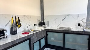 Uma cozinha moderna com fogão embutido, micro-ondas e torradeira. Há armários com portas de vidro e um painel de fundo em mármore.