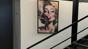 Uma escadaria com corrimão preto, parede branca e uma obra de arte emoldurada acima.