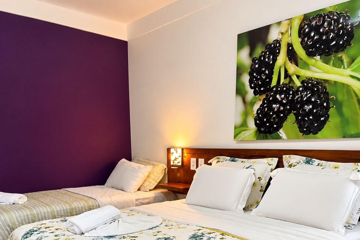 Quarto de hotel com uma cama grande, duas mesas de cabeceira e uma mesinha de noite com abajur.