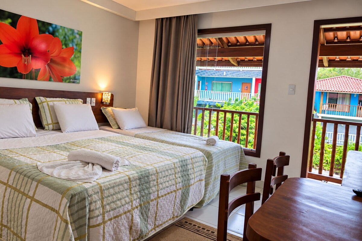 Quarto de hotel com cama grande, mesa de jantar e varanda com vista externa.