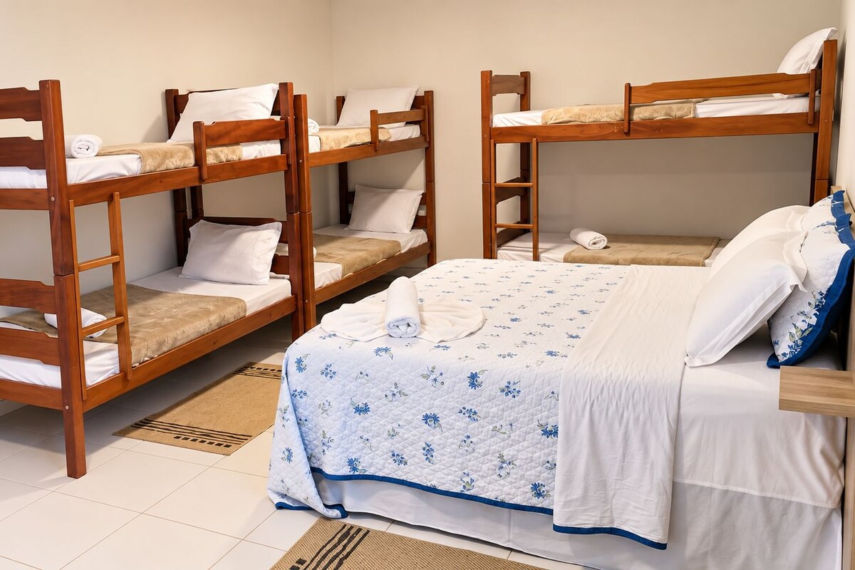 Quarto com beliches e uma cama de solteiro, com colcha e almofadas estampadas.