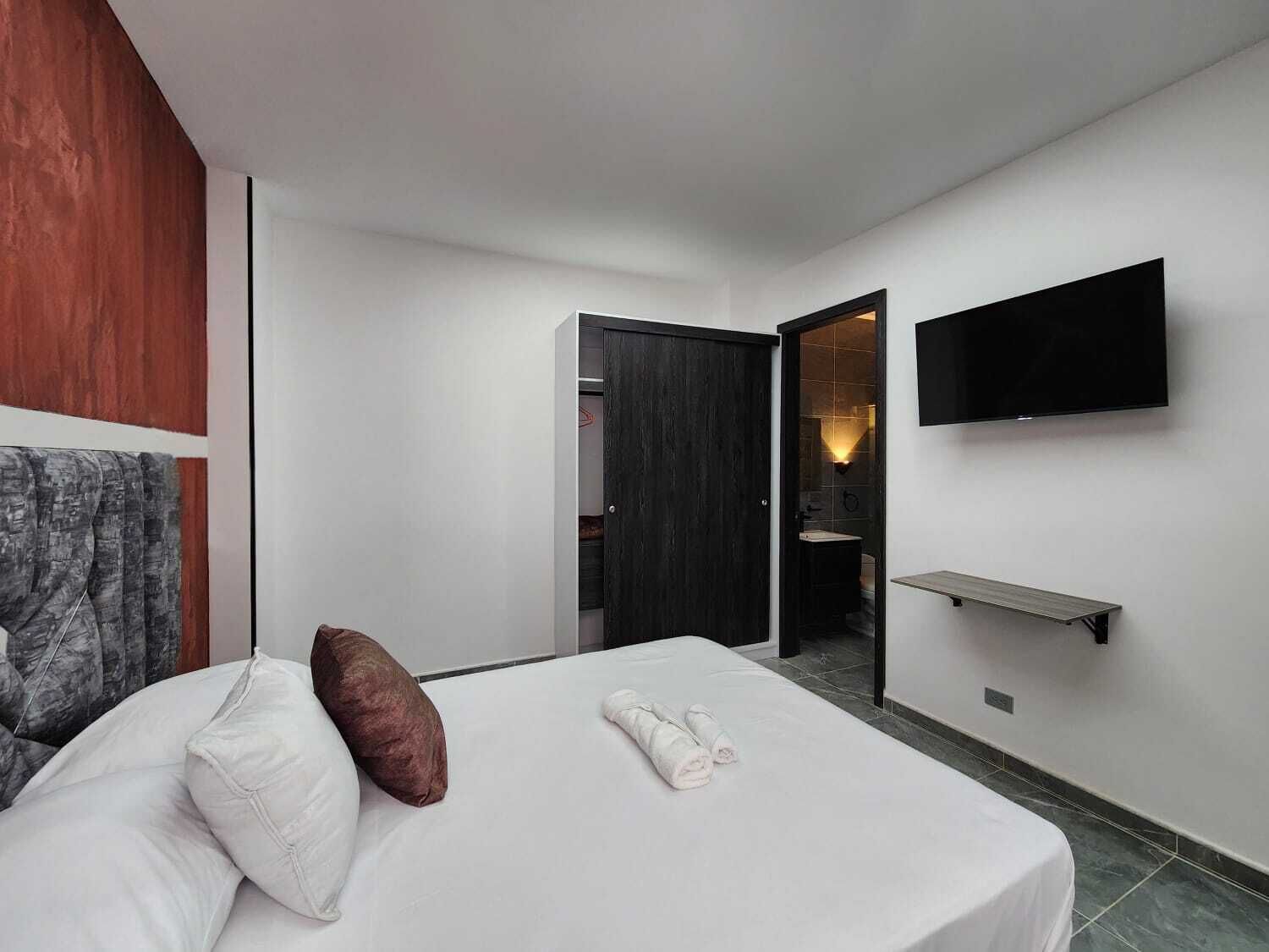 Quarto de hotel moderno com cama, televisão, banheiro e painel de parede em madeira.