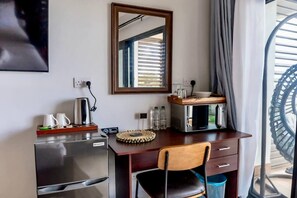 Quarto de hotel com cozinha compacta, escrivaninha, cadeira, espelho grande e vista para uma escada em caracol.