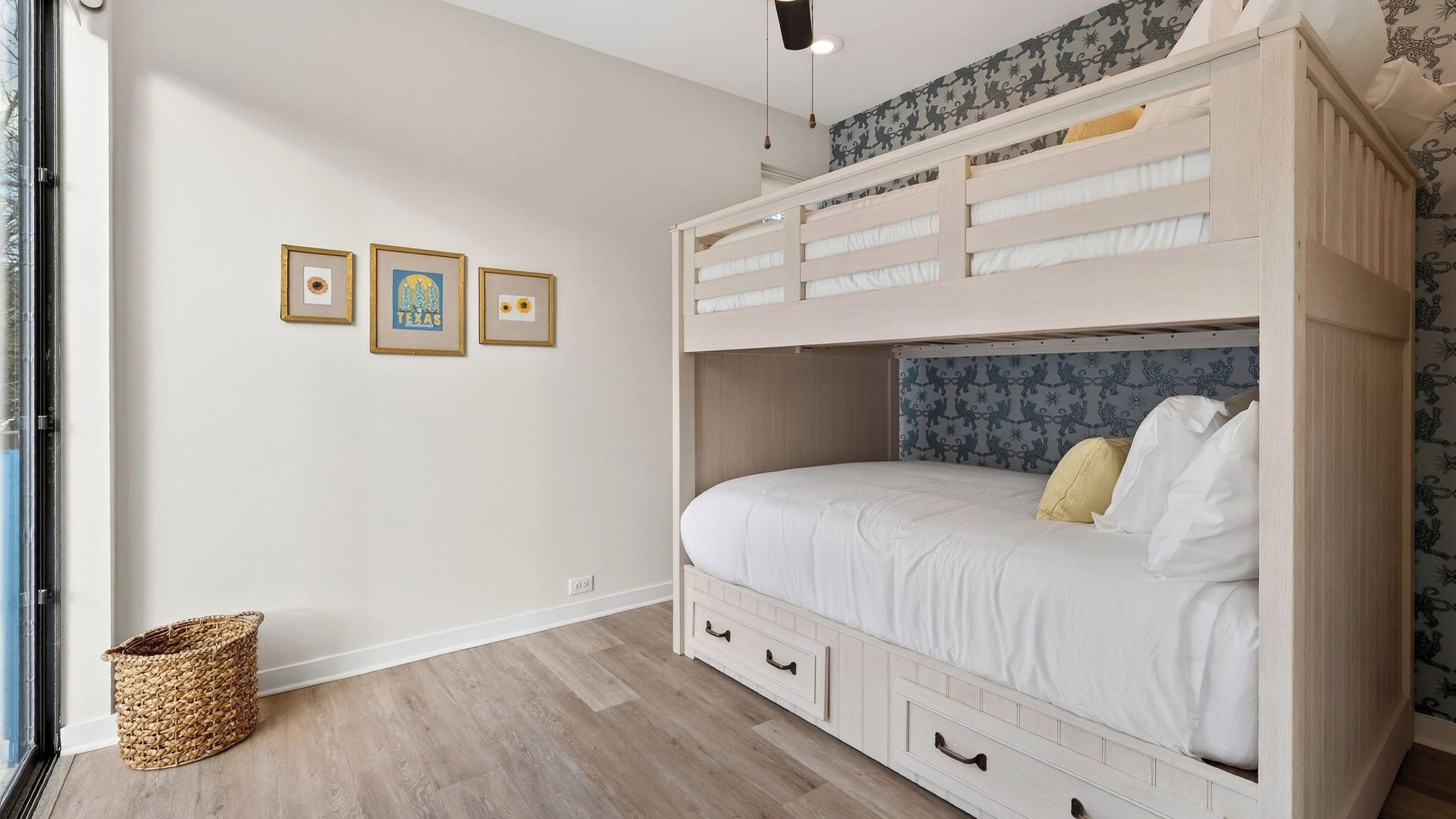 Uma cama box com beliche, uma cesta de palha e três quadros na parede.