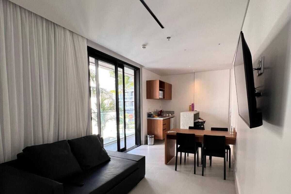 Uma sala de estar moderna com um sofá preto, um espaço de jantar com mesa e cadeiras, e uma cozinha com armários e bancada.