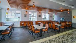 Um restaurante com mesas altas, áreas de cabines, janelas amplas e iluminação pendente.
