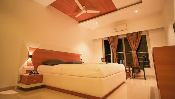 Quarto de hotel moderno com cama, mesa de cabeceira, abajur e ventoinha no teto.
