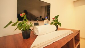 Uma mesa de madeira com uma toalha branca enrolada, duas plantas em vasos, uma garrafa e uma chaleira.