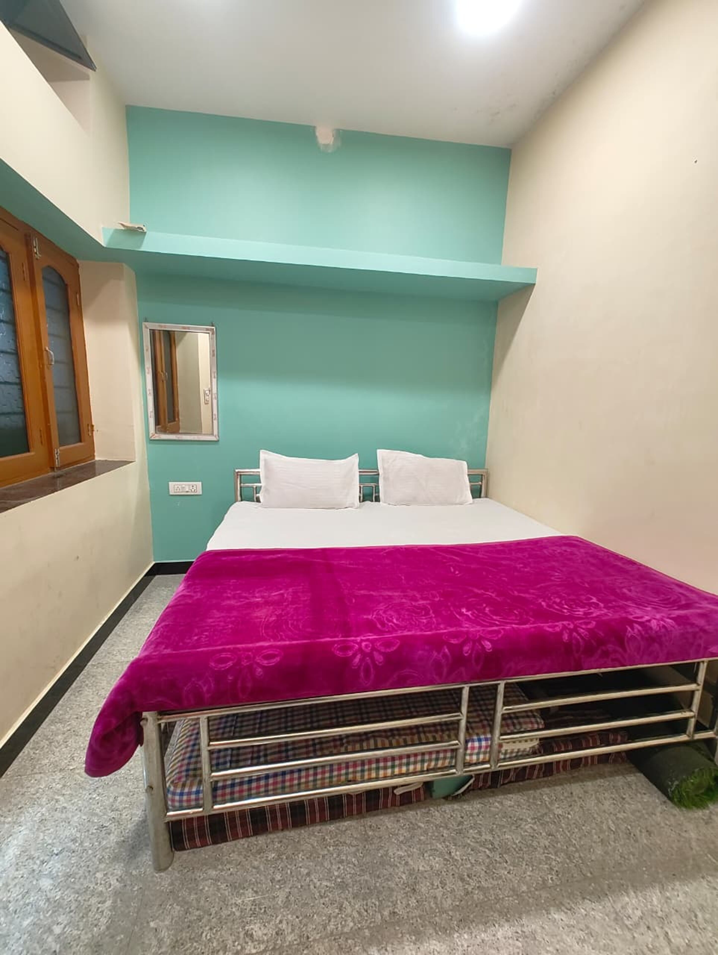 Quarto pequeno e estreito, com uma cama, janela e espelho.