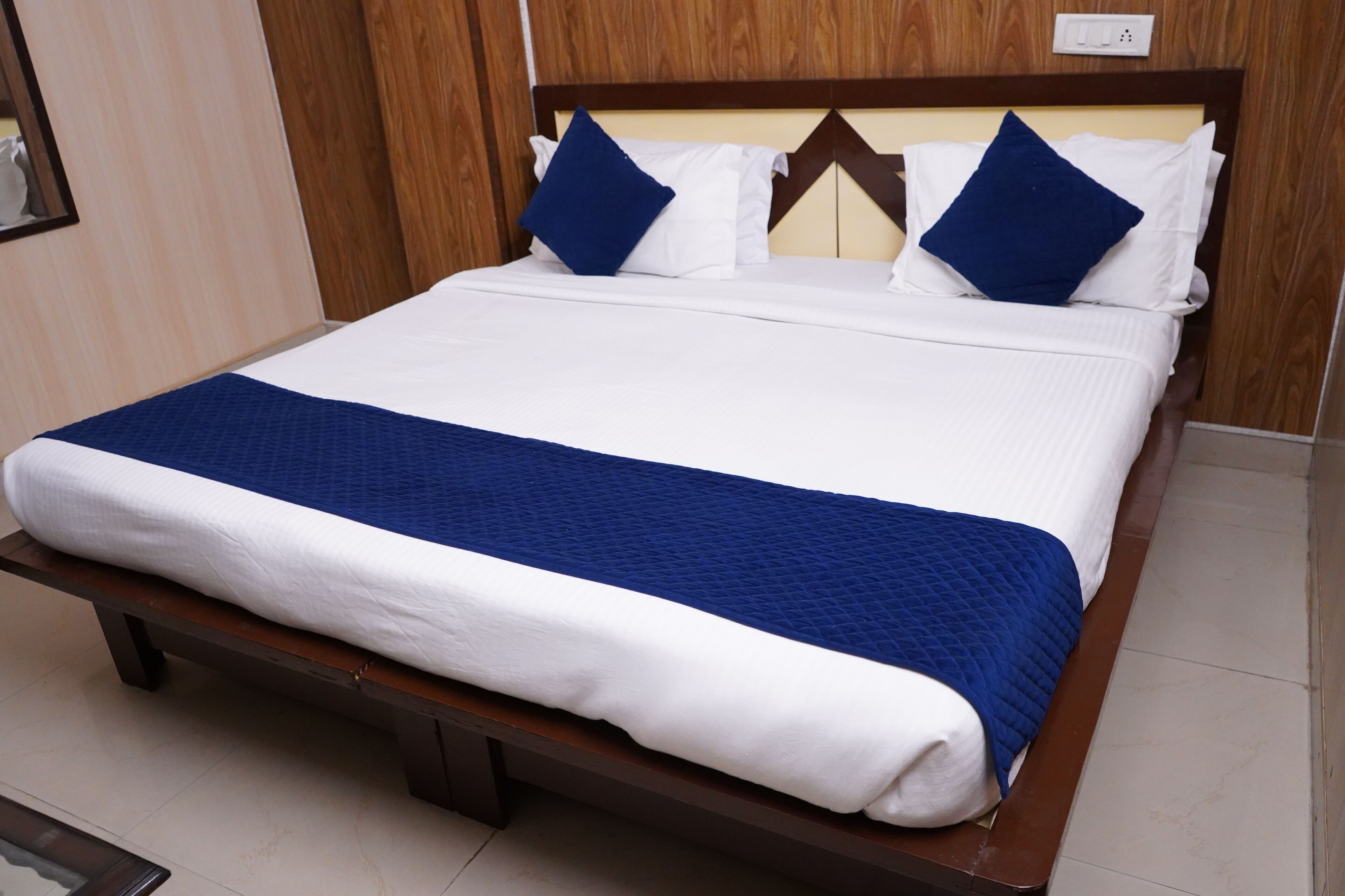 Cama bem arrumada com colcha azul, almofadas brancas e cabeceira de madeira.