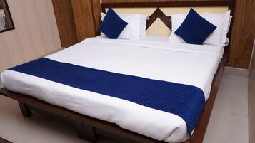 Cama bem arrumada com colcha azul, almofadas brancas e cabeceira de madeira.