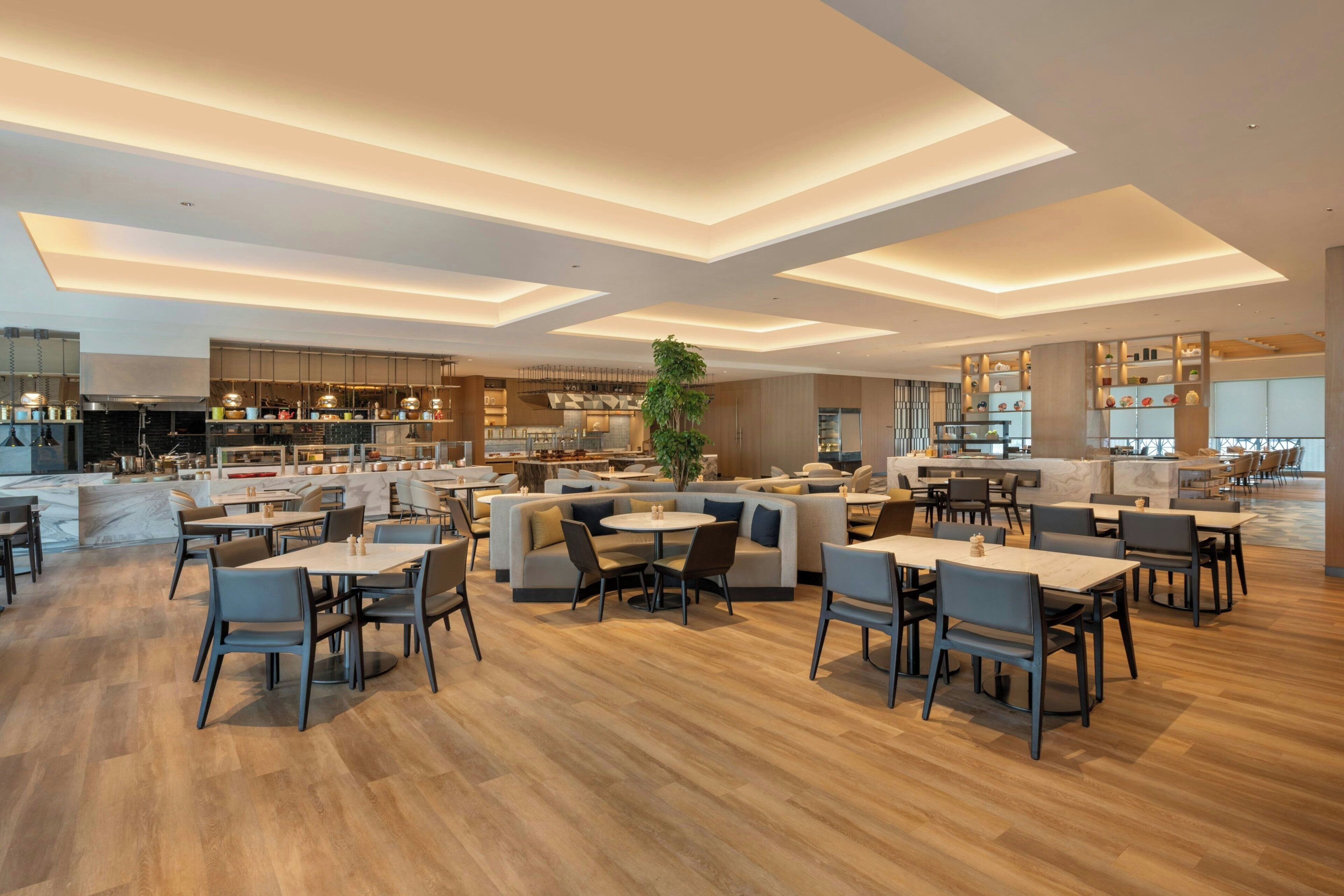 Restaurante moderno com área de estar central, bar e cozinha ao fundo.