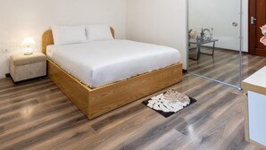 Quarto com cama, mesa de cabeceira, luminária, obra de arte e um separador de vidro que dá para o banheiro.
