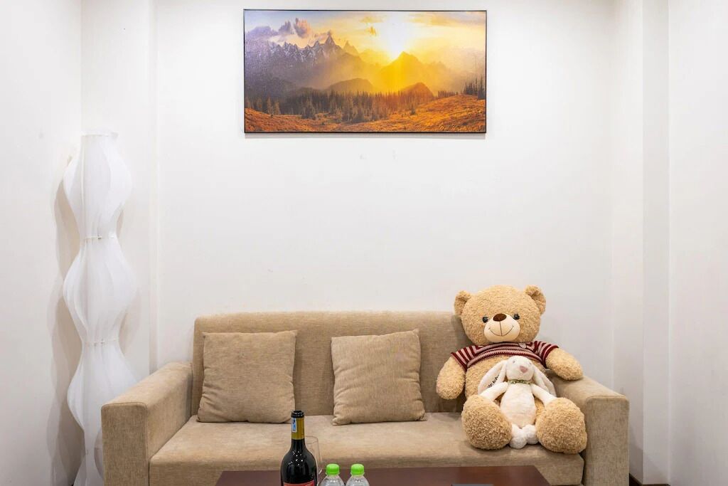 Um sofá bege com um urso de pelúcia e uma garrafa de vinho sobre uma mesa.
