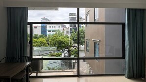 Quarto com uma grande porta de vidro deslizante que dá para uma varanda, uma mesa de jantar com cadeiras e vista para edifícios e áreas verdes.