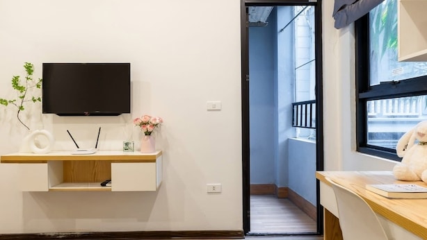 Quarto de hotel moderno com televisão de tela plana, escrivaninha, cama e piso de madeira.