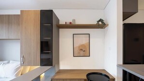 Quarto moderno com cama, escrivaninha, cadeira, prateleira com objetos decorativos e um quadro na parede.