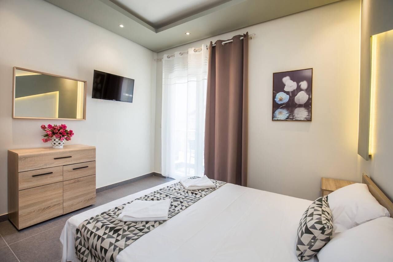 Quarto de hotel com cama, televisão, penteadeira, espelho e um quadro.