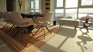 Uma sala de jantar moderna com uma mesa de vidro, quatro cadeiras, um banco e janelas amplas com vista.
