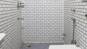 Casa de banho com azulejos brancos tipo metrô, chuveiro, sanita e lavatório.