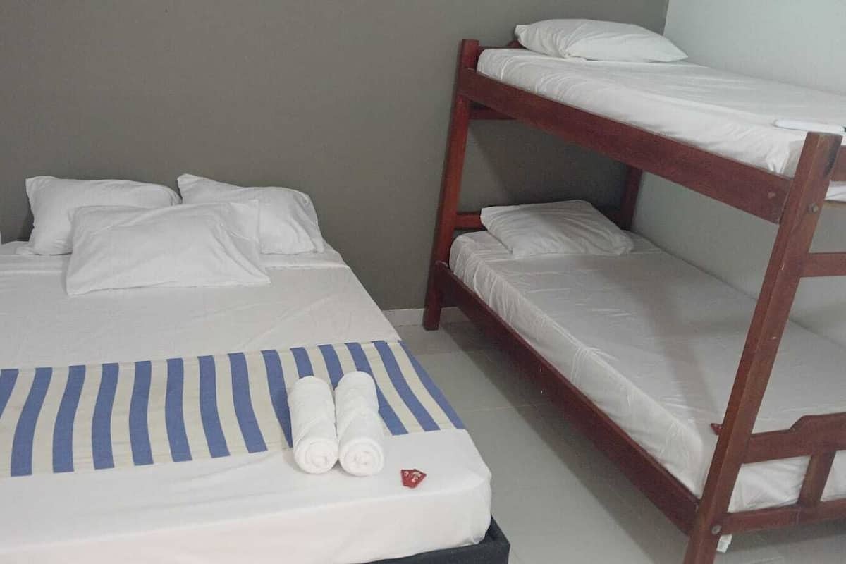 Uma cama de solte com um cobertor listrado e duas toalhas enroladas, uma cama beliche e um pequeno objeto vermelho na cama.