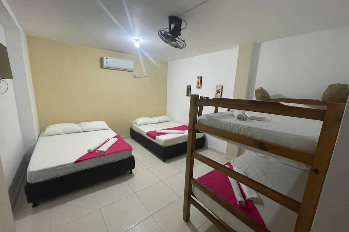 Um quarto com beliches, ventilador de teto, ar condicionado e piso ladrilhado.