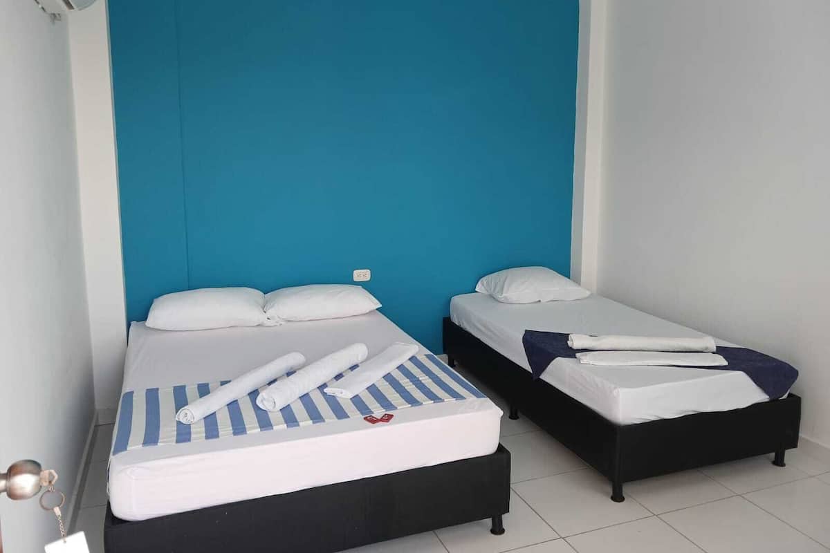 Quarto com duas camas, uma com colcha listrada e a outra com colcha branca lisa.