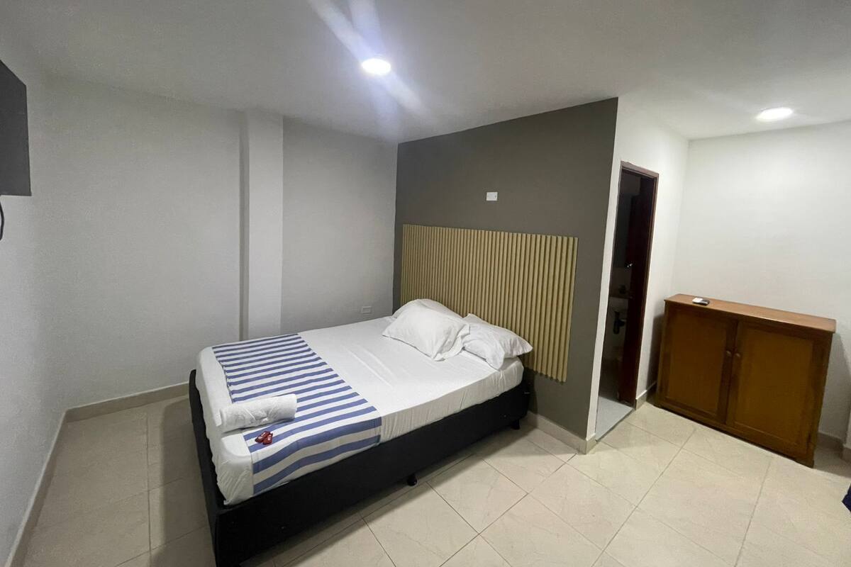 Quarto de hotel com cama, mesa de cabeceira, guarda-roupa e porta.