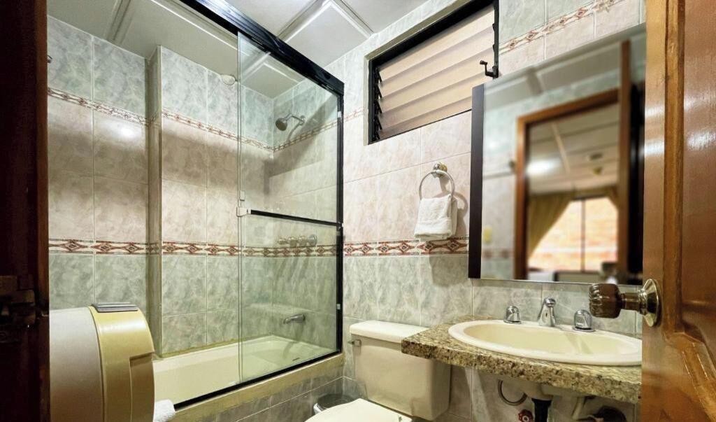 Casa de banho com chuveiro em cabine de vidro, sanita, lavatório com espelho e porta-toalhas.