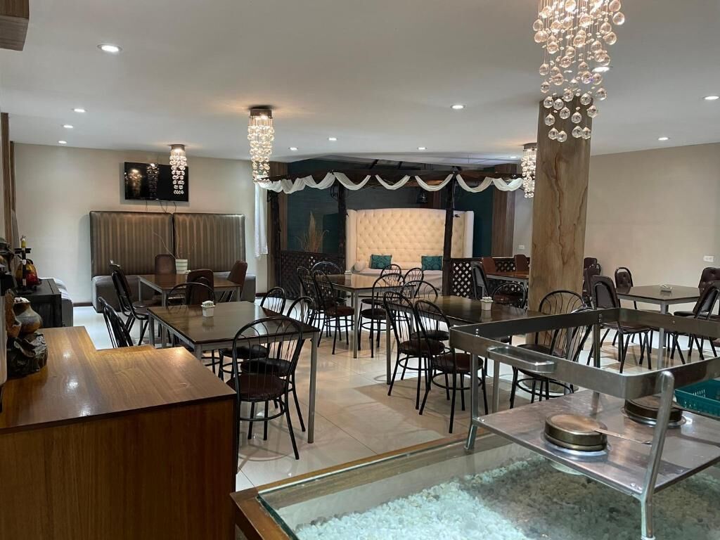Uma sala de jantar moderna com várias mesas e cadeiras, uma coluna de madeira grande e lustres decorativos.