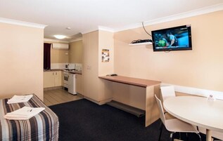 Quarto de hotel compacto com cozinha compacta, área de refeições, TV fixada na parede e cama com manta listrada.