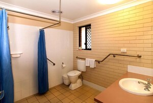 Casa de banho com sanita branca, cortina de chuveiro azul, lavatório com espelho e janela com grade de metal.