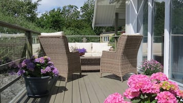 Um deck de madeira com móveis de vime e vasos de flores.