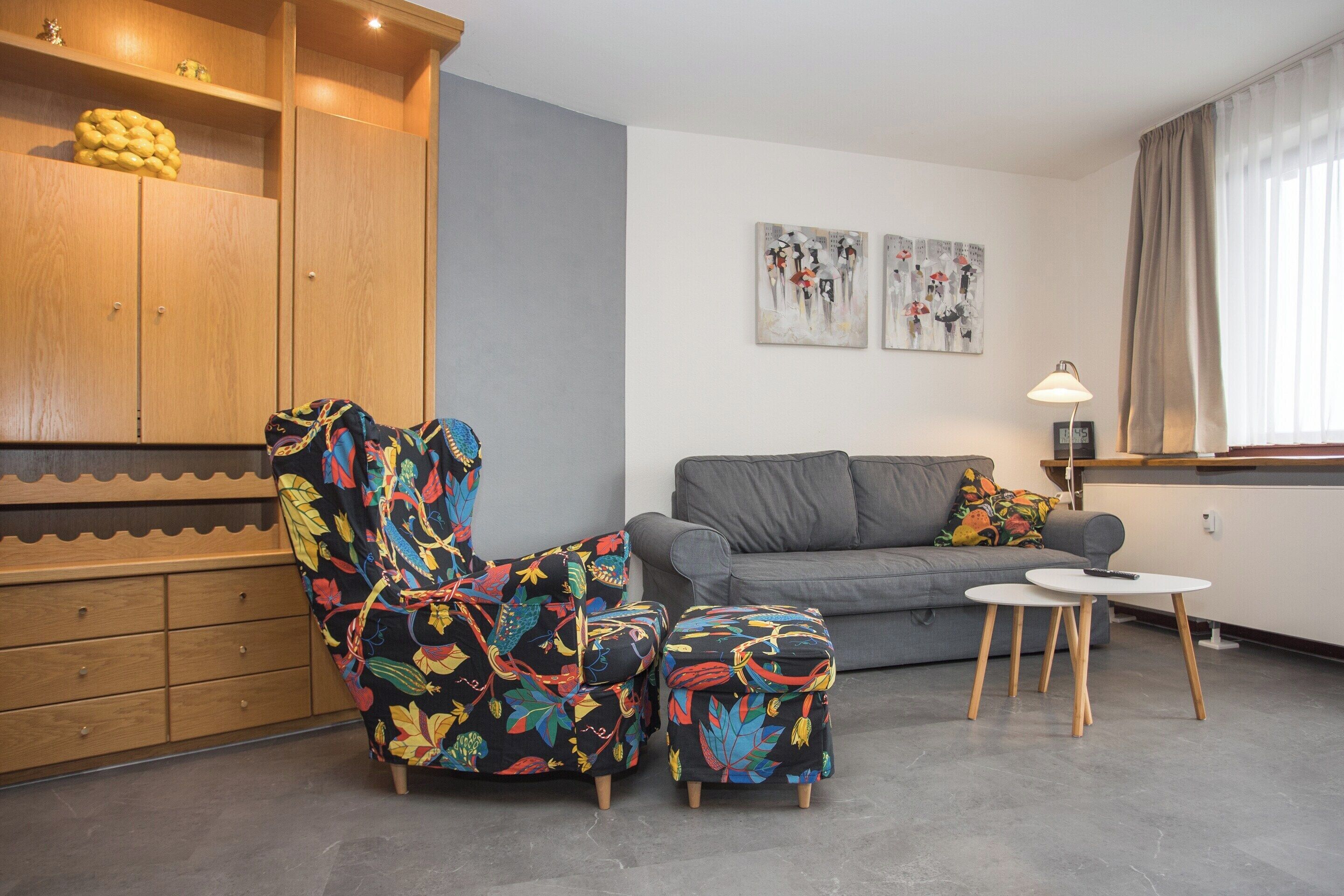 Uma sala de estar com sofá, mesa de centro, poltrona estampada e aparador de madeira.