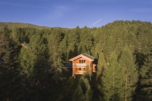Uma cabana de madeira rodeada por floresta densa, erguida sobre pilares, com uma varanda com vista para as árvores.