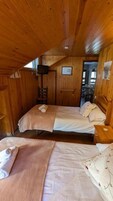Quarto de cabana de madeira com duas camas, uma cadeira, uma escrivaninha e uma televisão.