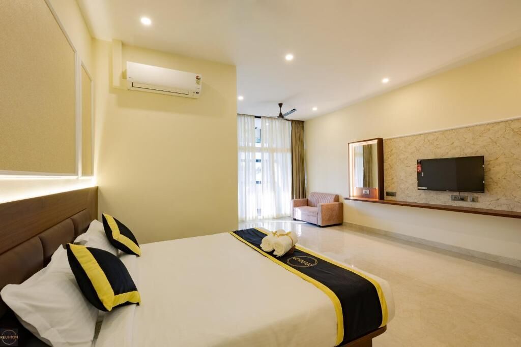 Quarto de hotel com cama, televisão, ventoinha no teto e janela com cortinas.
