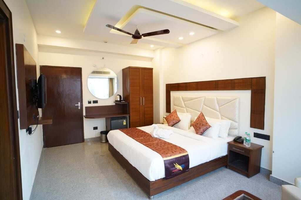 Quarto de hotel com uma cama, um ventilador de teto, um guarda-roupa de madeira, um espelho e uma pequena mesa de cabeceira.