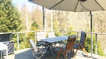 Um deck externo com mesa e cadeiras, um guarda-sol grande e vista para as árvores.