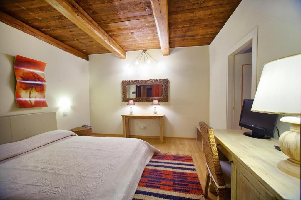 Quarto com cama, escrivaninha, computador, espelho e luminária.