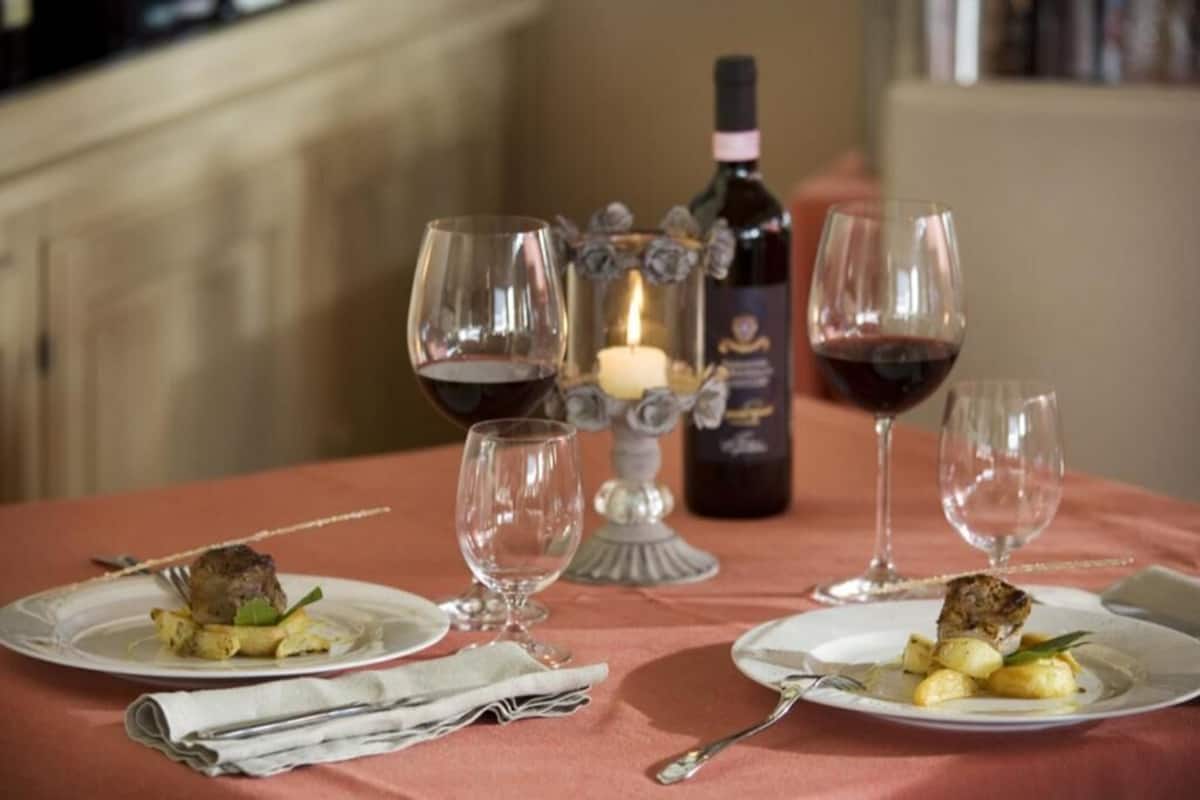 Mesa posta para dois, com pratos de comida, copos de vinho e um castiçal como centro.