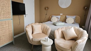 Quarto com cama, duas poltronas, uma mesinha, televisão e um ornamento circular na parede.