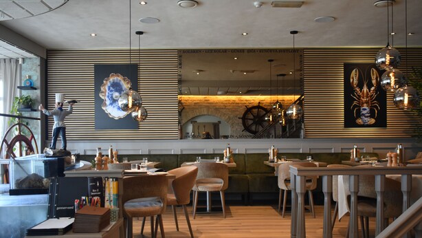 Interior de restaurante com piso de madeira, móveis modernos e decoração na parede.