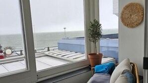 Varanda com vista para o mar, um sofá de vime, uma planta em vaso e um objeto decorativo na parede.