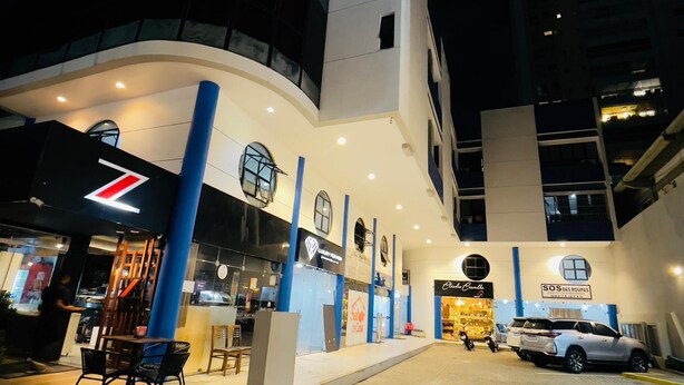 Um edifício com fachada curva, entrada visível e área pavimentada com um carro estacionado.