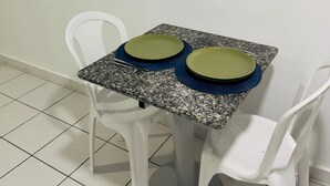 Uma área de refeições com televisão na parede, duas cadeiras brancas, uma mesa de granito e dois pratos verdes.